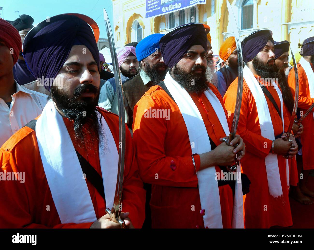 Sikh pilgrims in traditional dress hold ceremonial swords during a ...