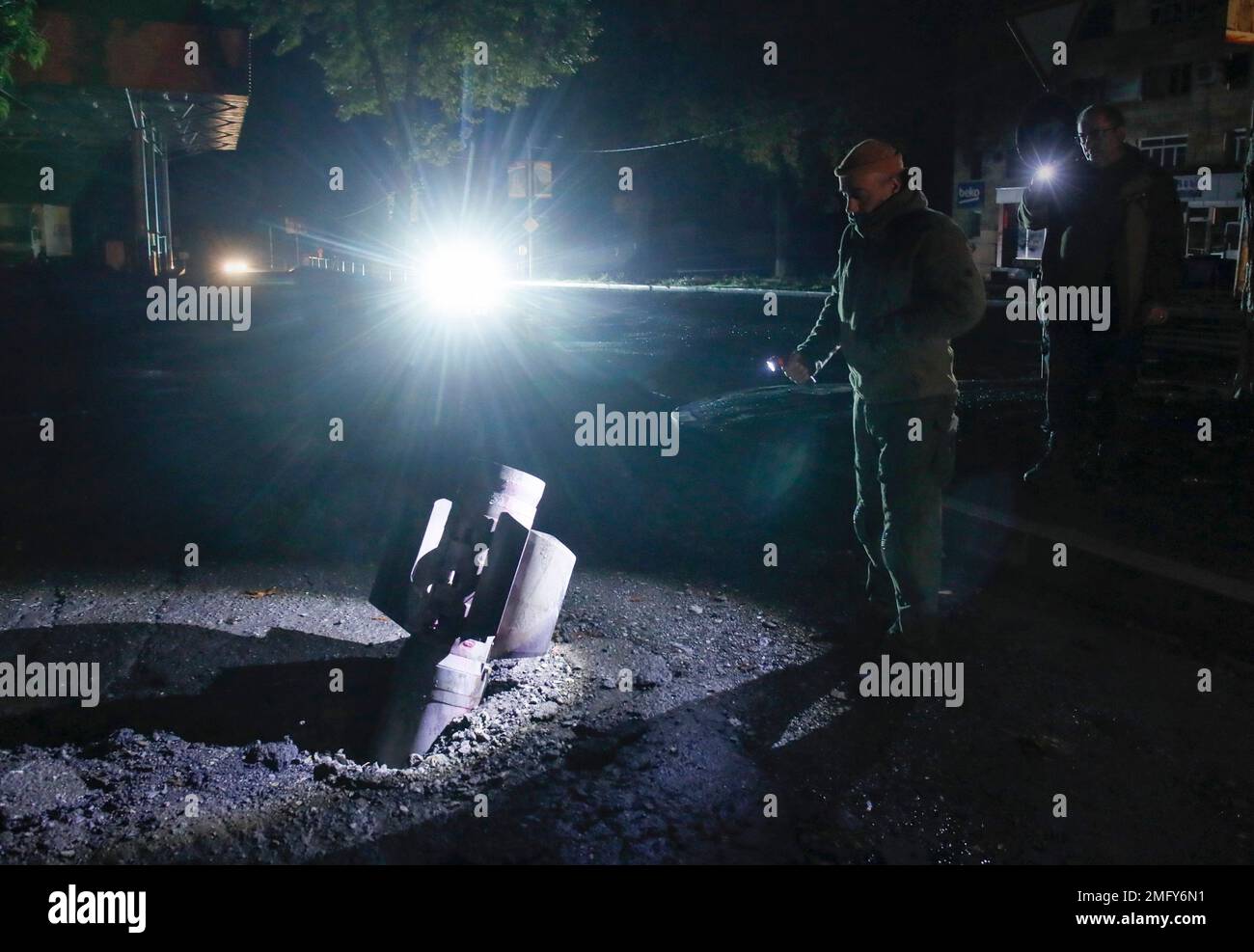 Men inspect an unexploded projectile of a multiple rocket launcher ...