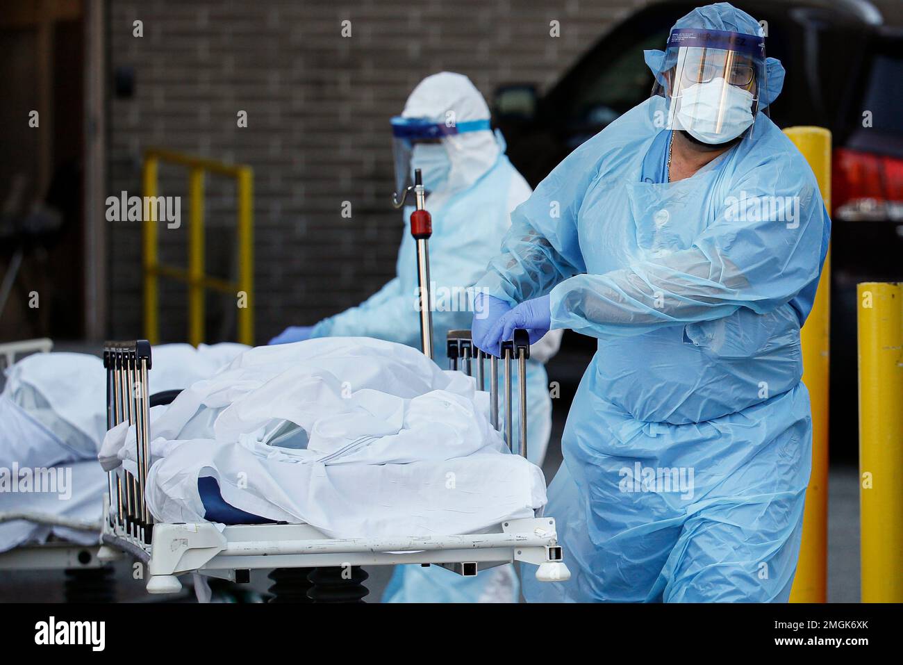 Medical workers wearing personal protective equipment wheel bodies to a ...