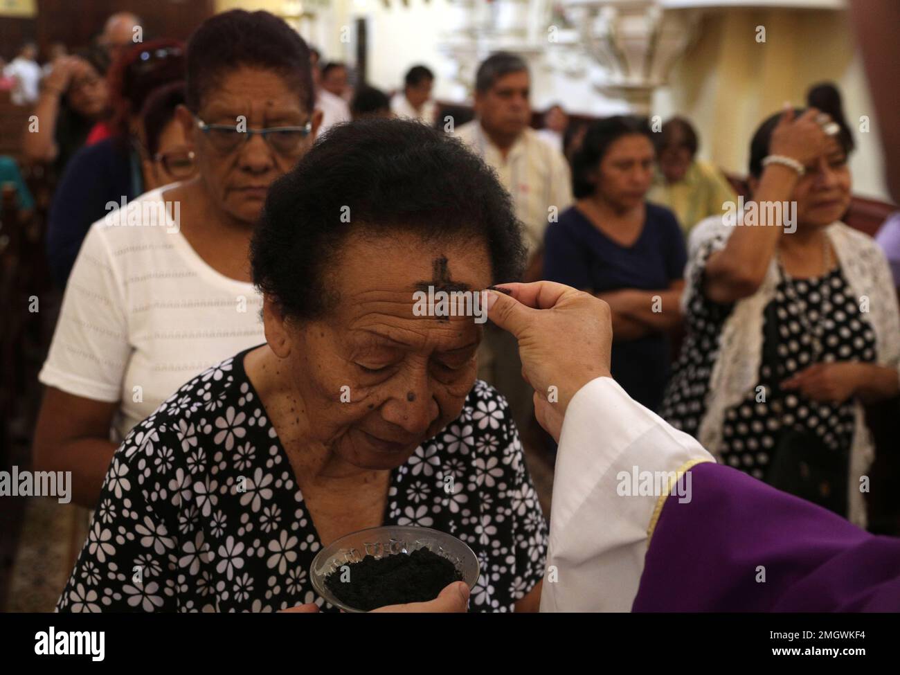 A priest marks the forehead of a woman with the symbol of a cross ...