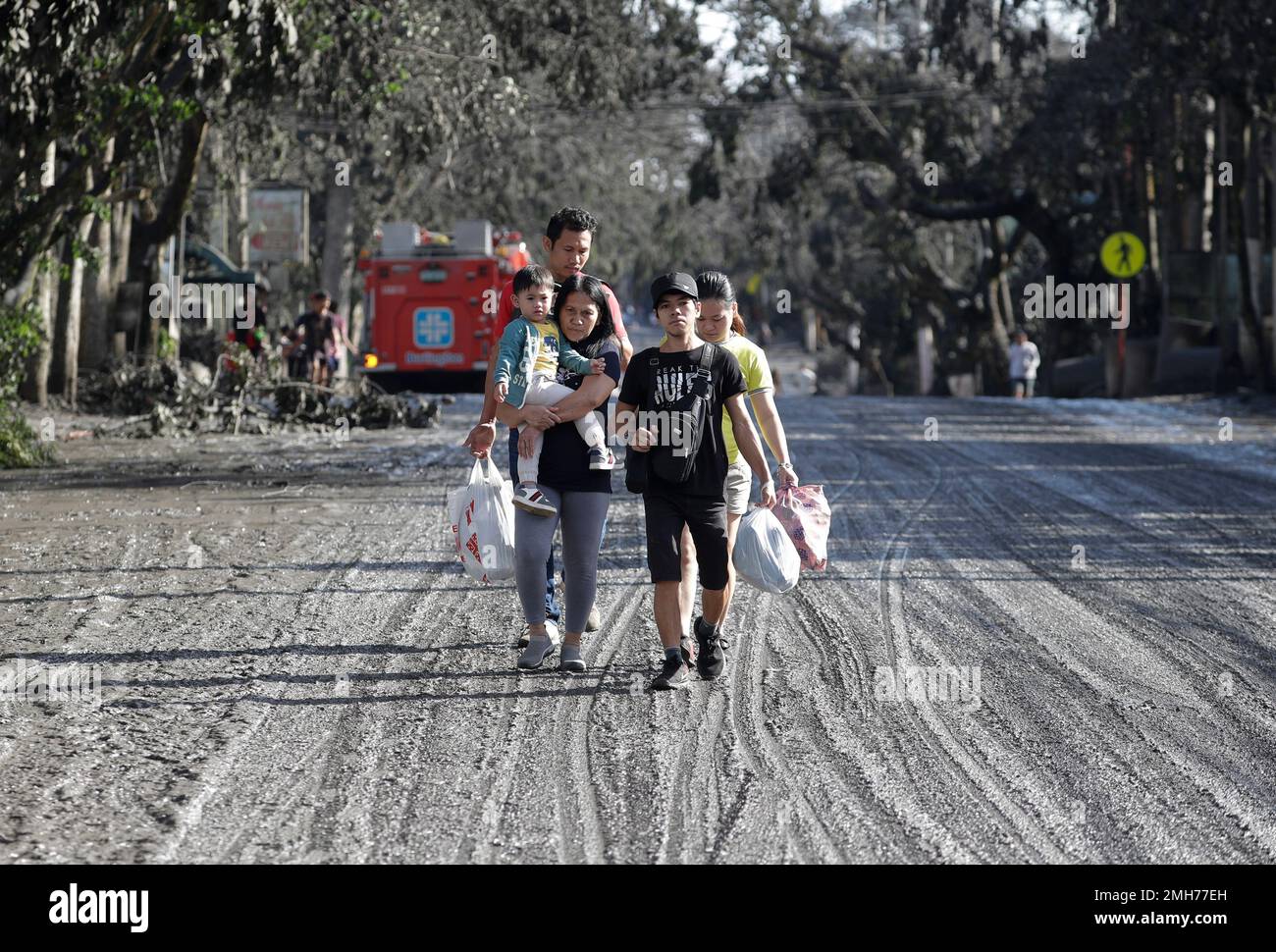 A family walks along a road covered with ash from Taal volcano in ...