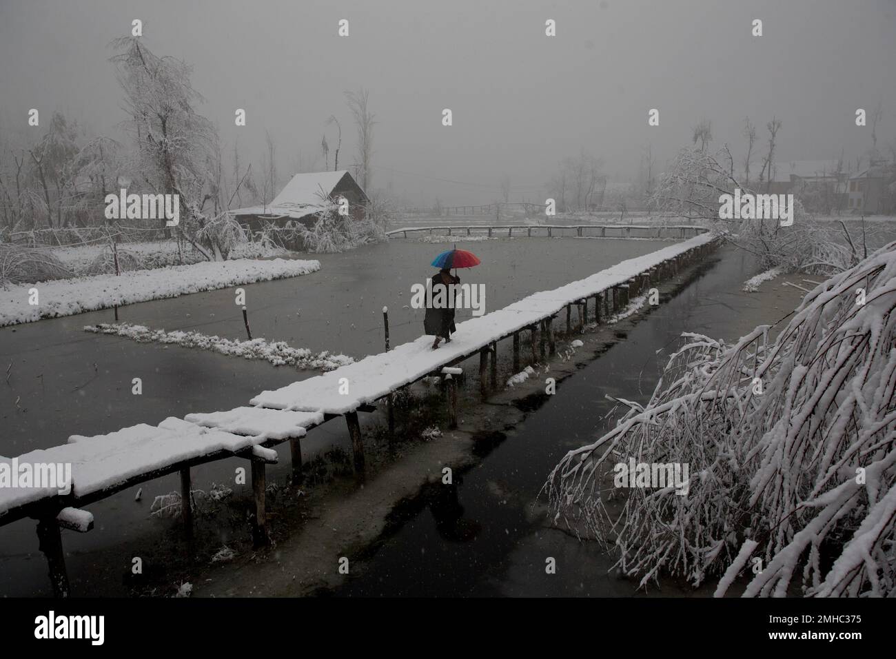 A Kashmiri man walks on a snow covered foot bridge as it snows in the ...