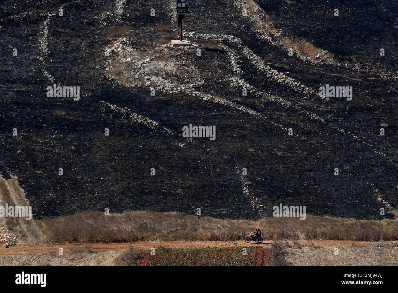 Lebanese men ride their motorcycle past fields that burned from Israeli ...