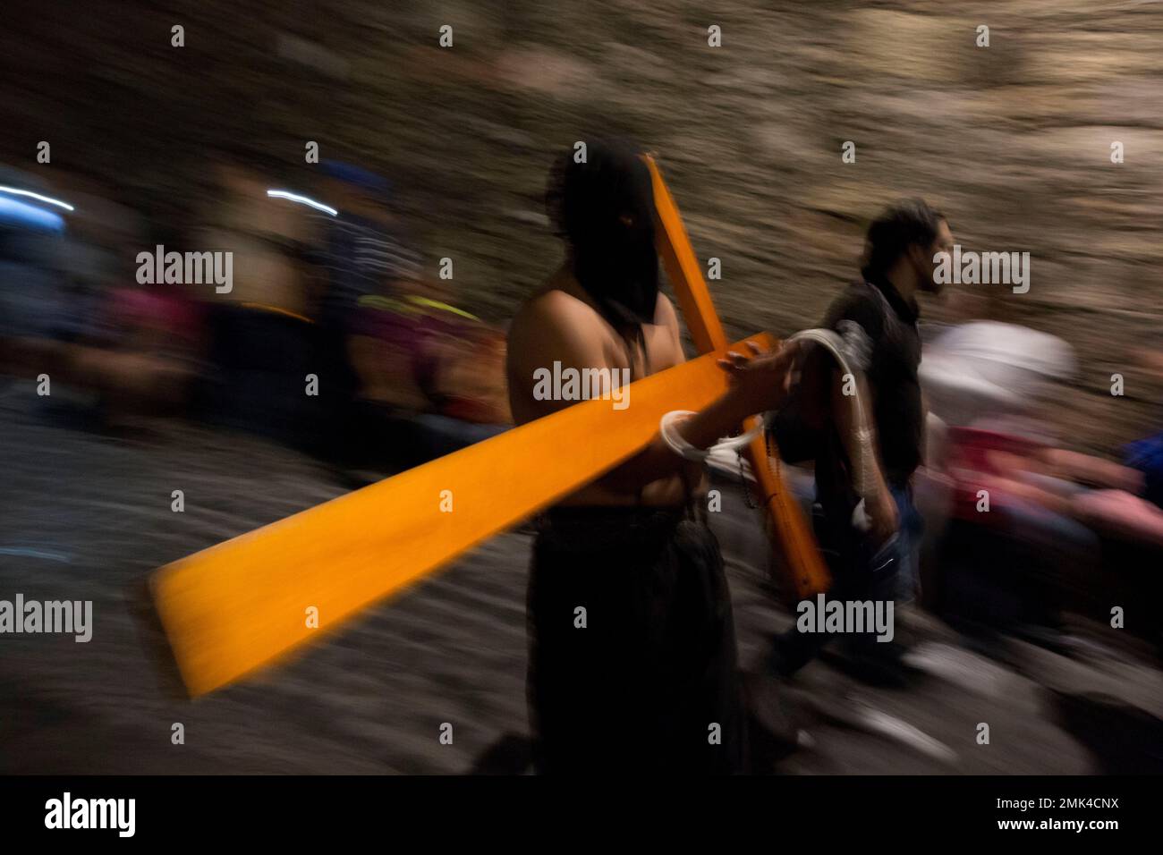A penitent carries a cross and a nail-studded whip as he walks in a ...