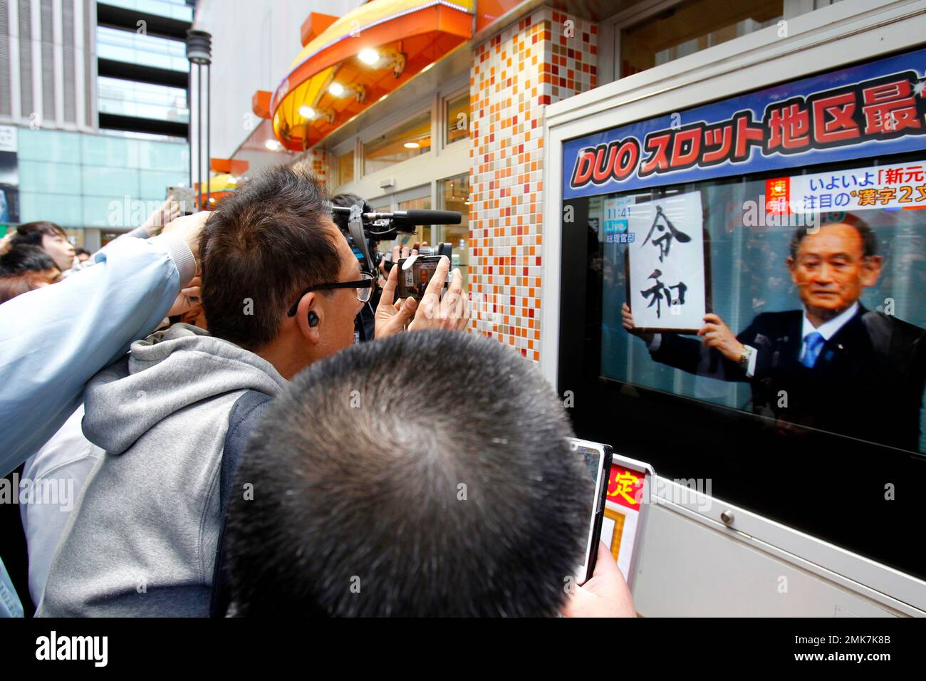 People look at a TV screen showing Japan’s Chief Cabinet Secretary ...