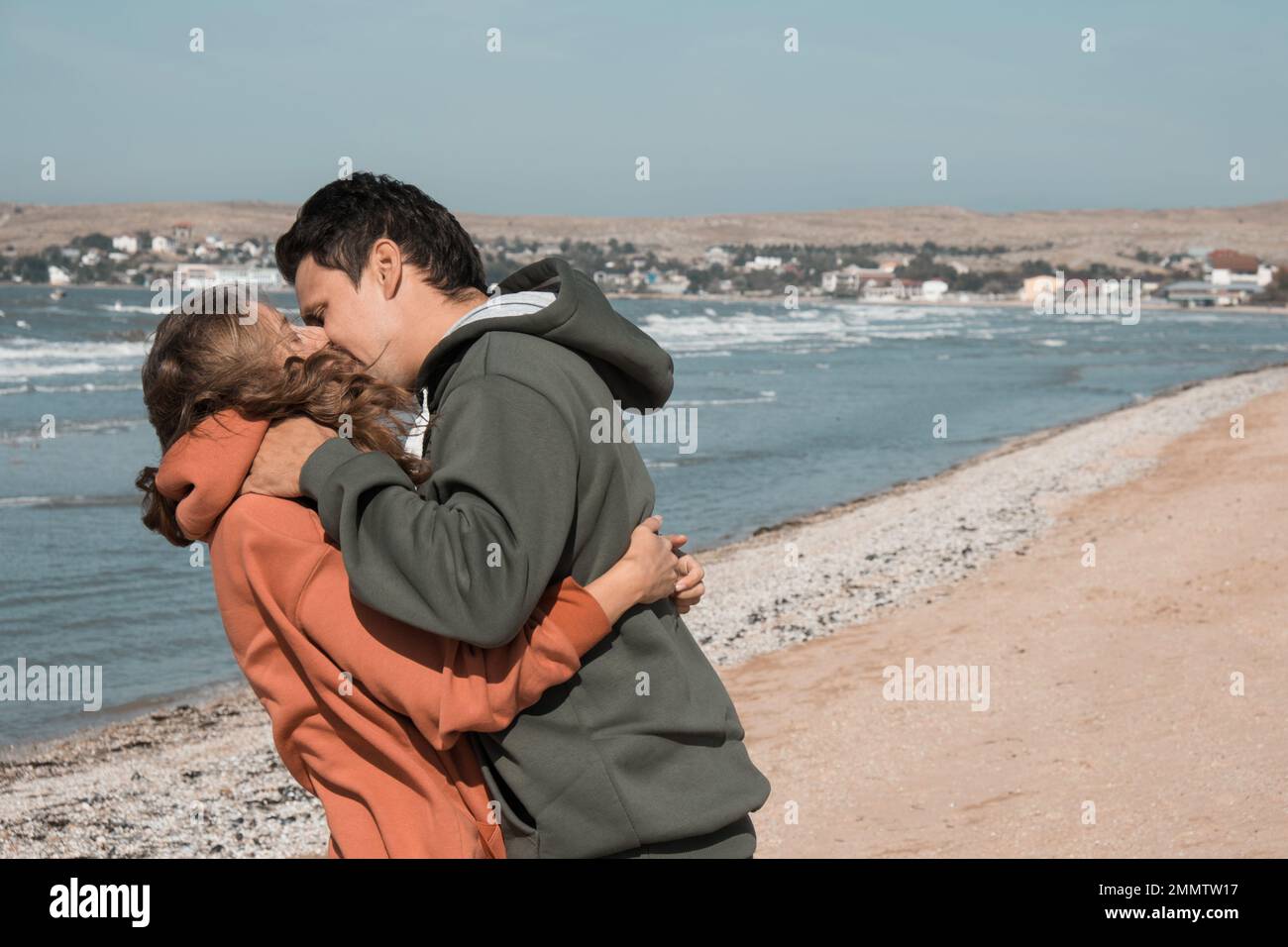 Der Typ und das Mädchen umarmen sich und sehen sich liebevoll am Strand an, vor dem Hintergrund ...