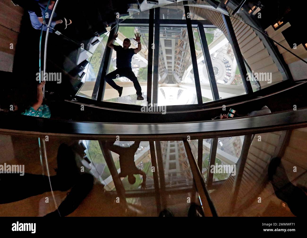 A man lies atop a glass floor, reflected in windows adjacent to it, at ...