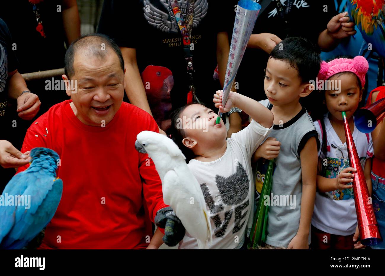 Zoo owner Manny Tangco, holds Macaw parrots while children blow paper horns as they join in a ...