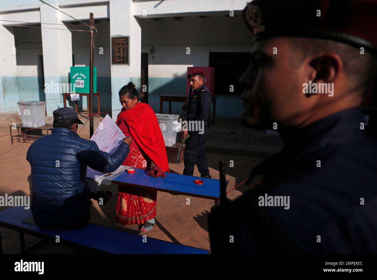A Nepalese policeman stands guard as a woman receives ballot paper from ...