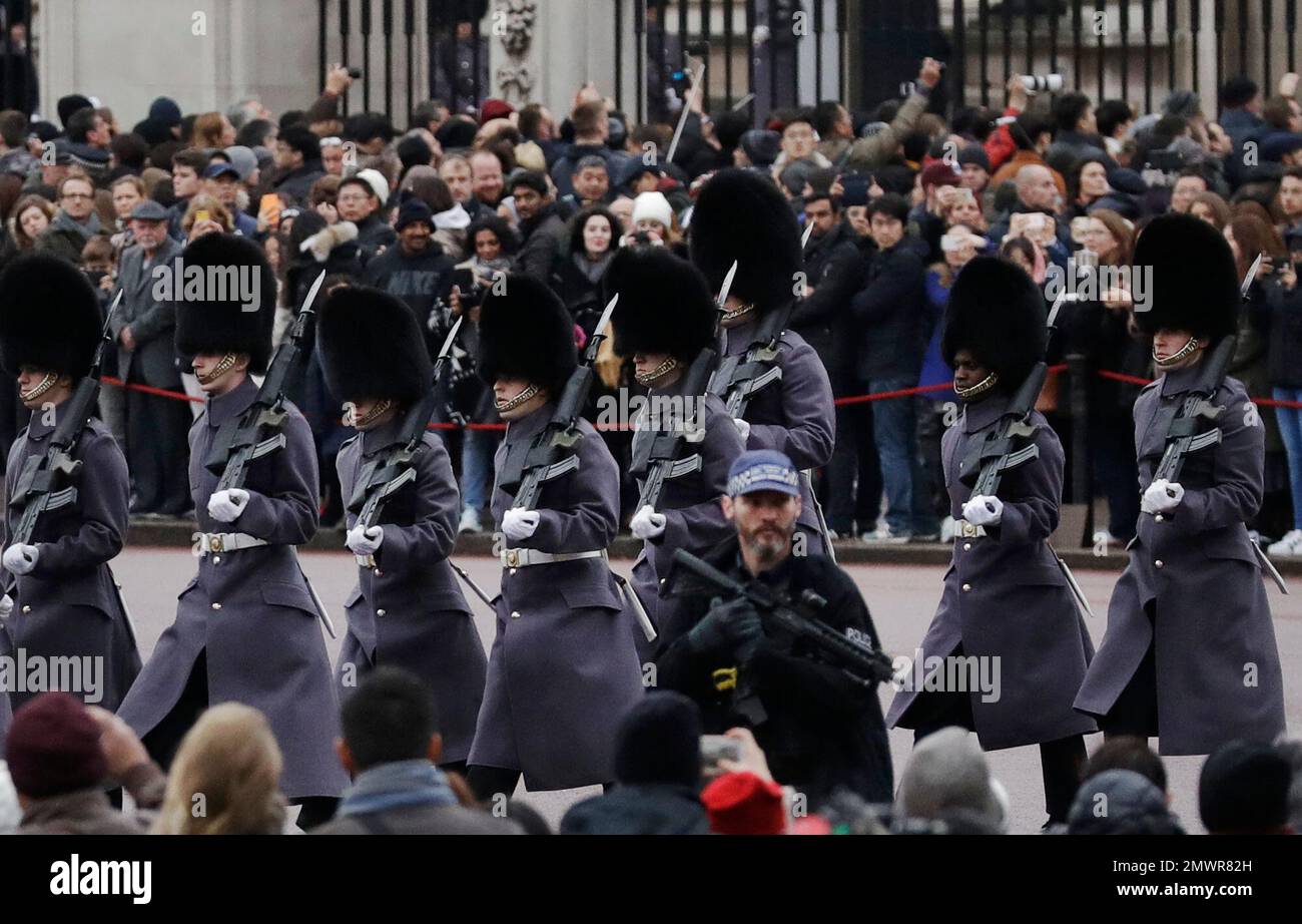 An armed police officer stands guard in the foreground as members of ...