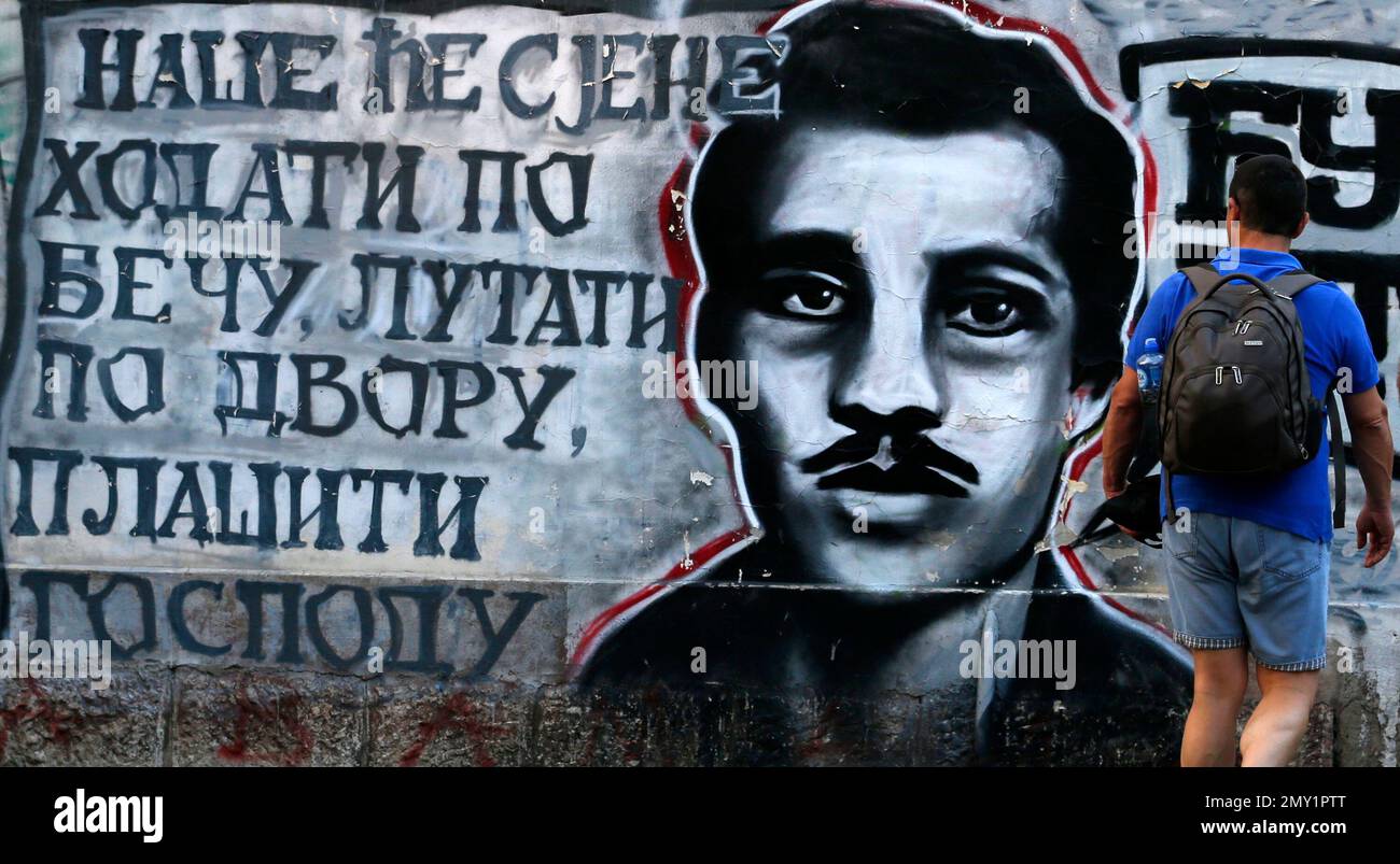 A man walks past graffiti on a wall showing Gavrilo Princip, the ...