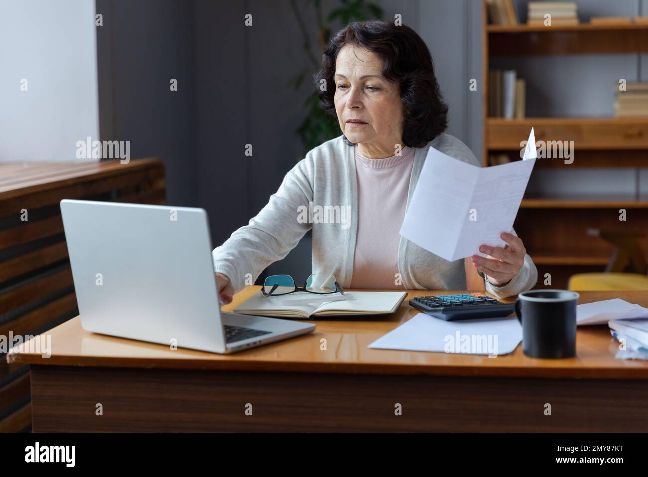 Eine ältere Frau im mittleren Alter sitzt mit einem Laptop und einem ...