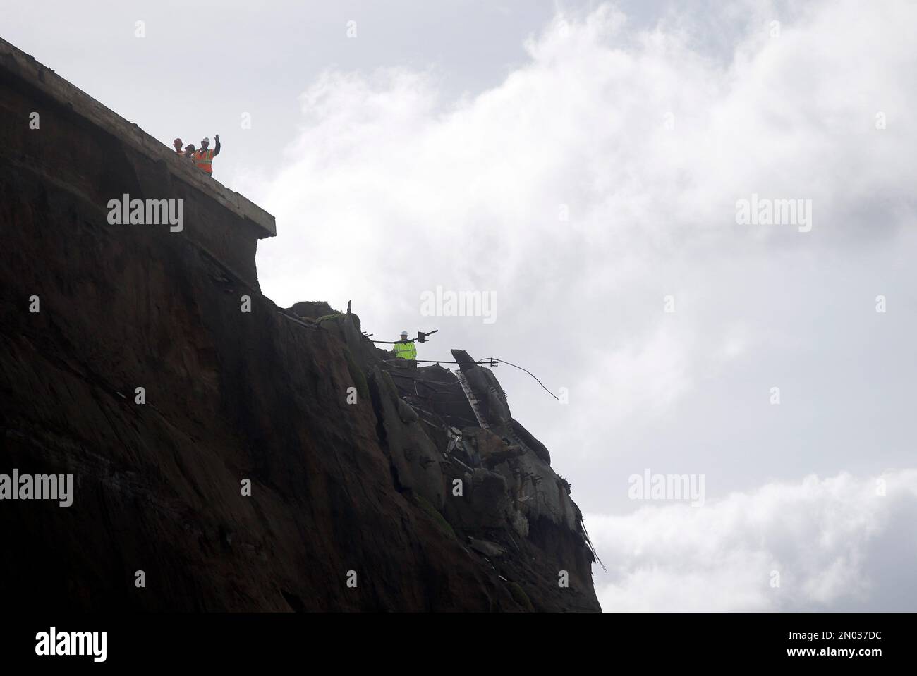 Construction crews stand atop a cliffside as an apartment building is ...