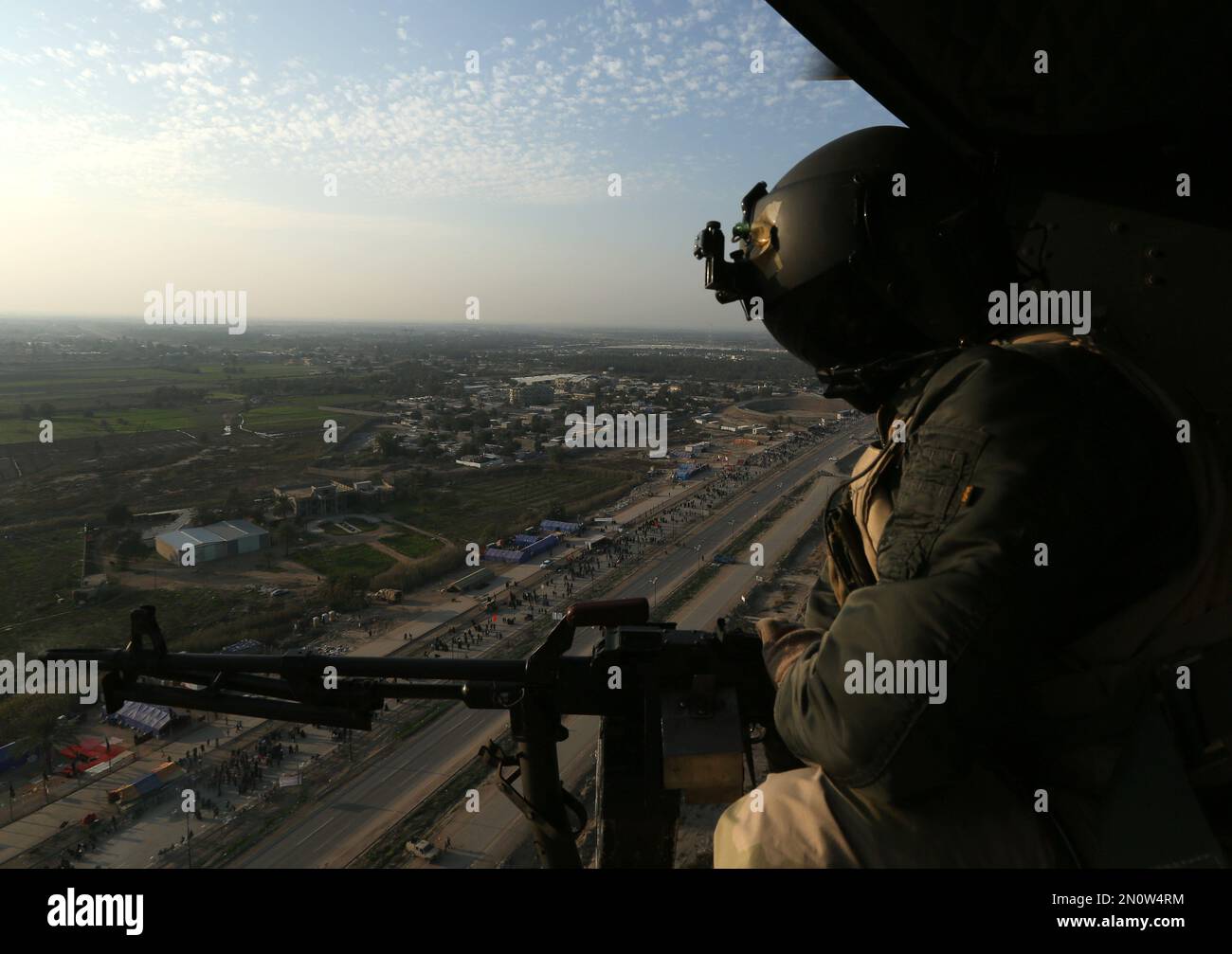 An Iraqi Army soldier in a helicopter flies high above Shiite pilgrims ...