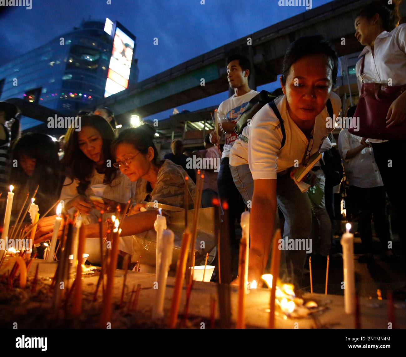 Thai people place lighted candles at the Erawan Shrine for the victims ...