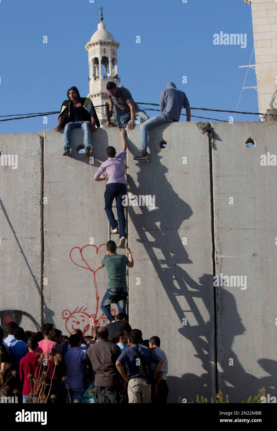 Palestinians use a ladder to climb over the separation barrier with ...