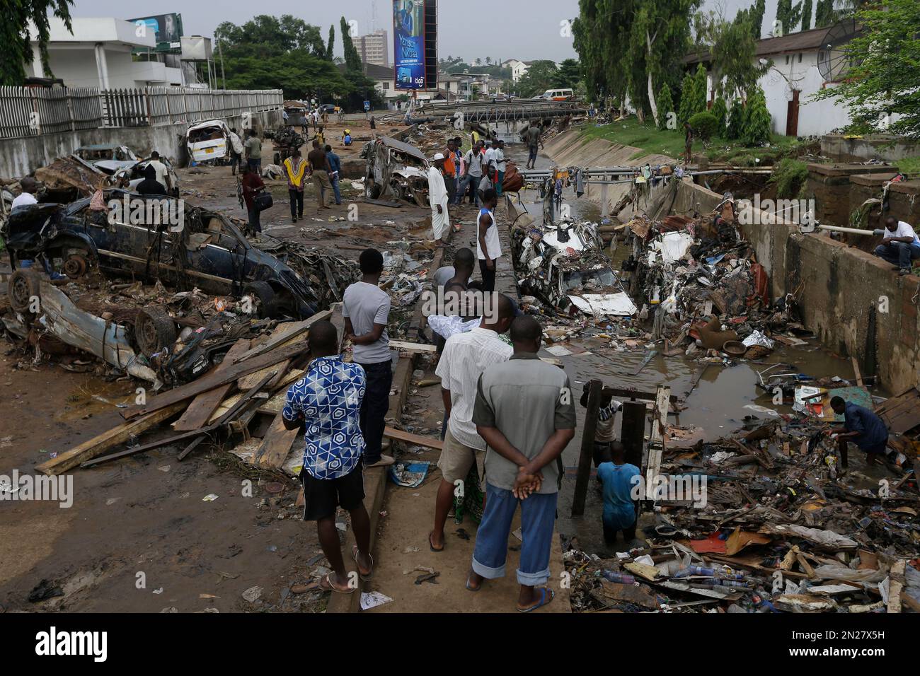 People gather around destroyed cars swept into a gully by flash floods ...
