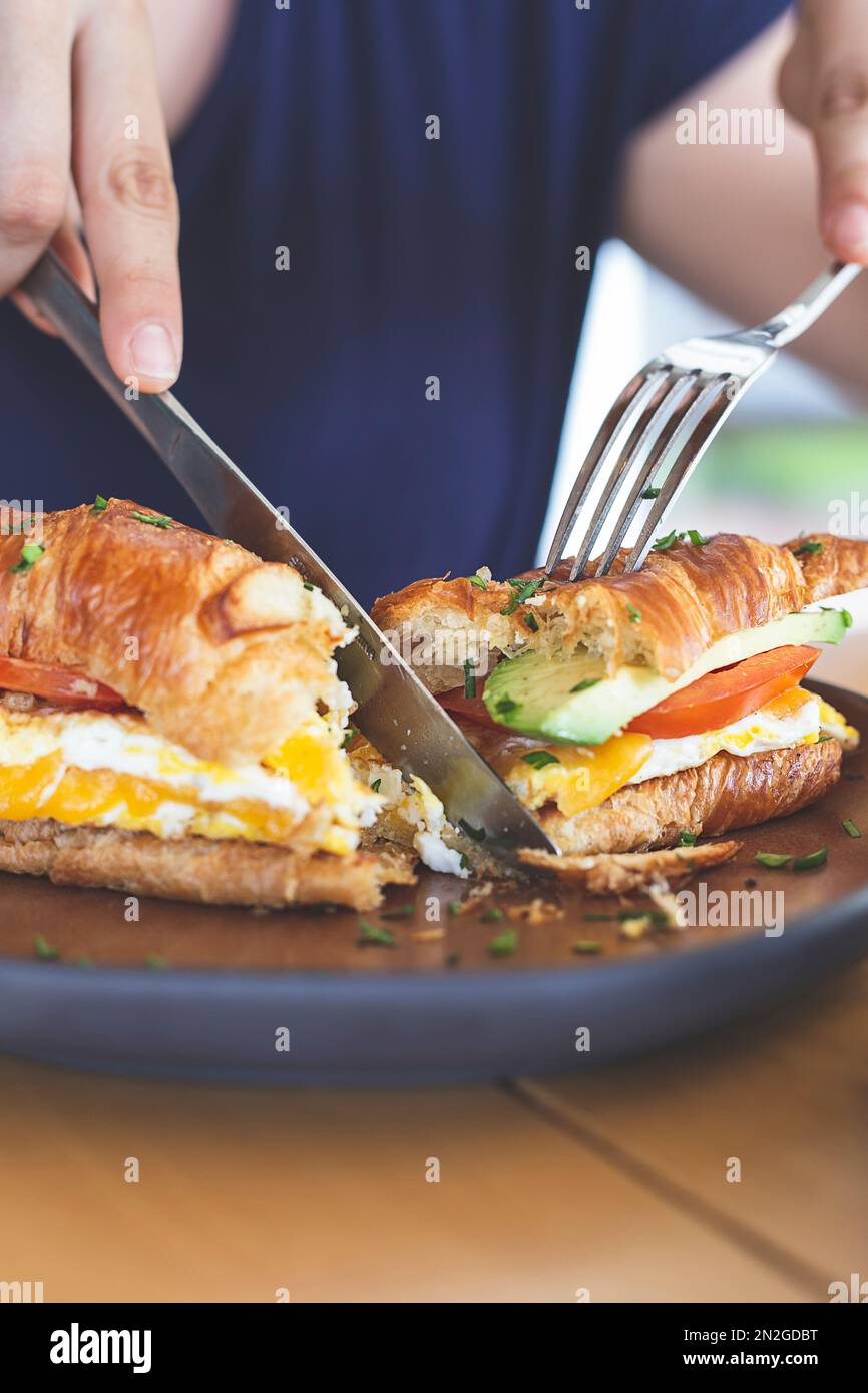 Hände halten Messer und Gabel und schneiden ein Croissant gefüllt mit ...