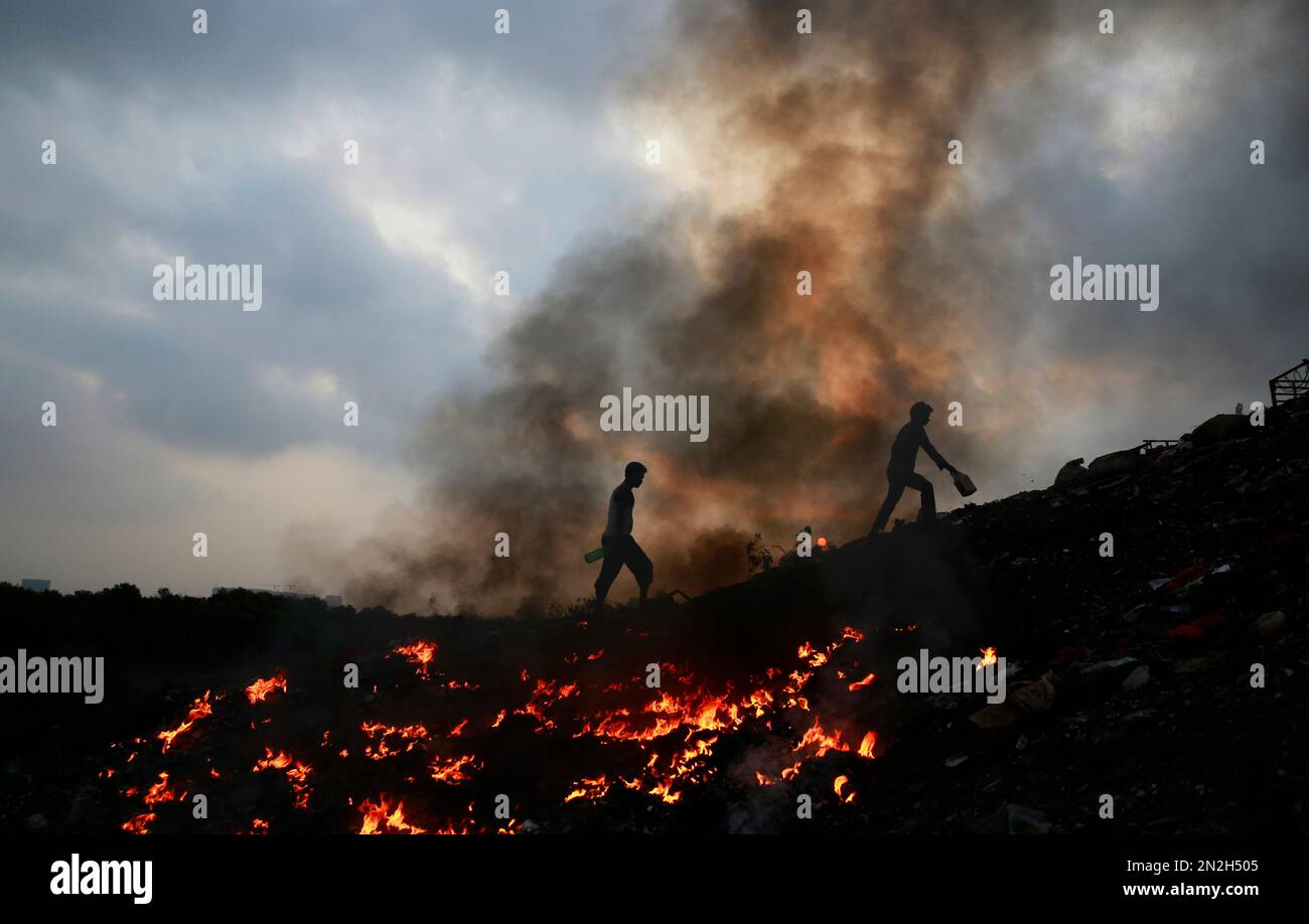 In this April 9, 2015 photo, impoverished Indians walk next to burning ...