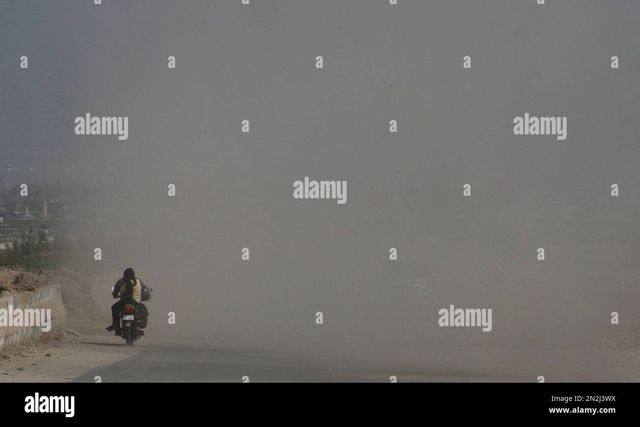 An Indian couple rides a motorcycle through a dusty road in New Delhi ...