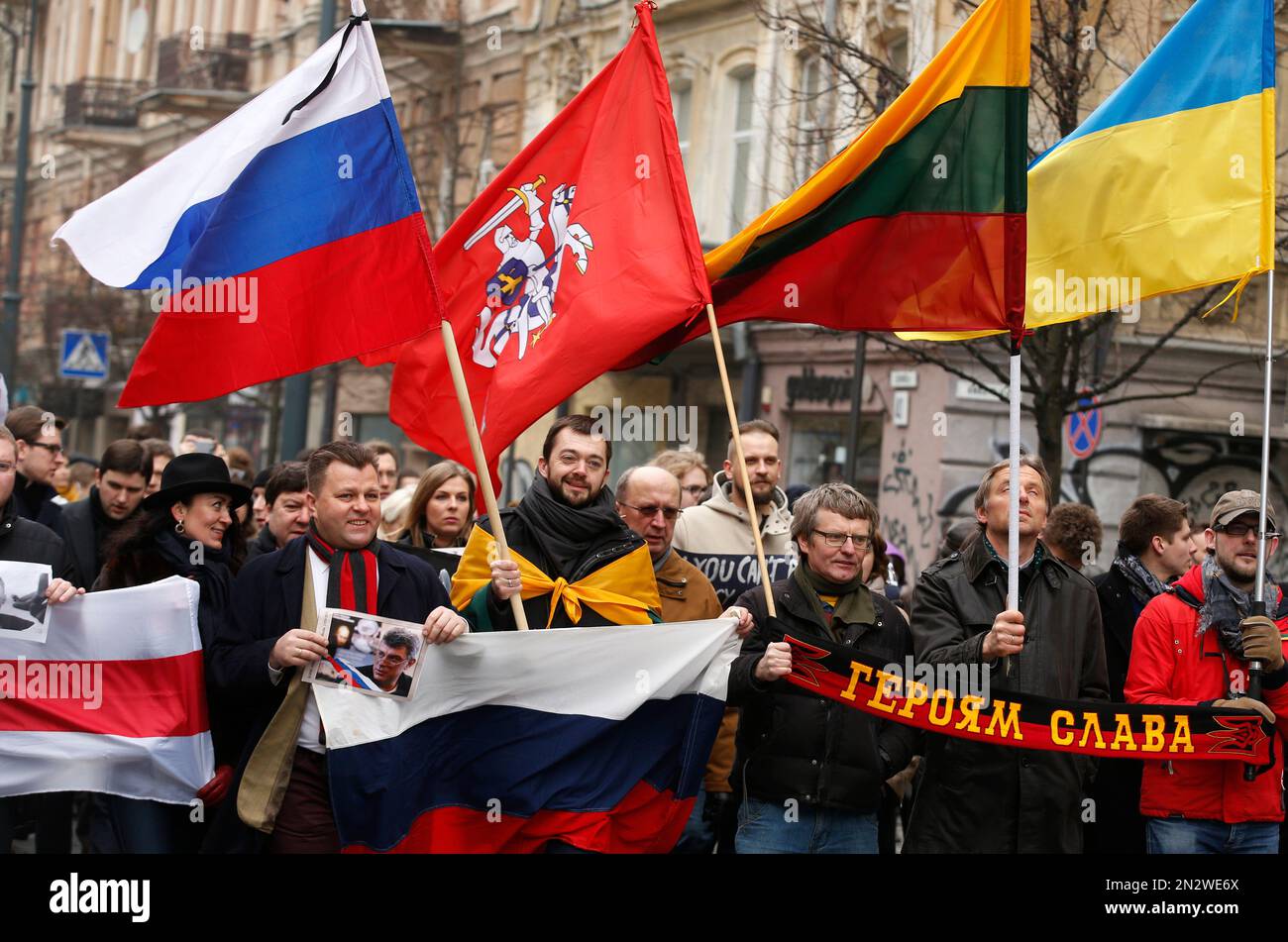 People march with various flags, including the Russian flag at left and ...
