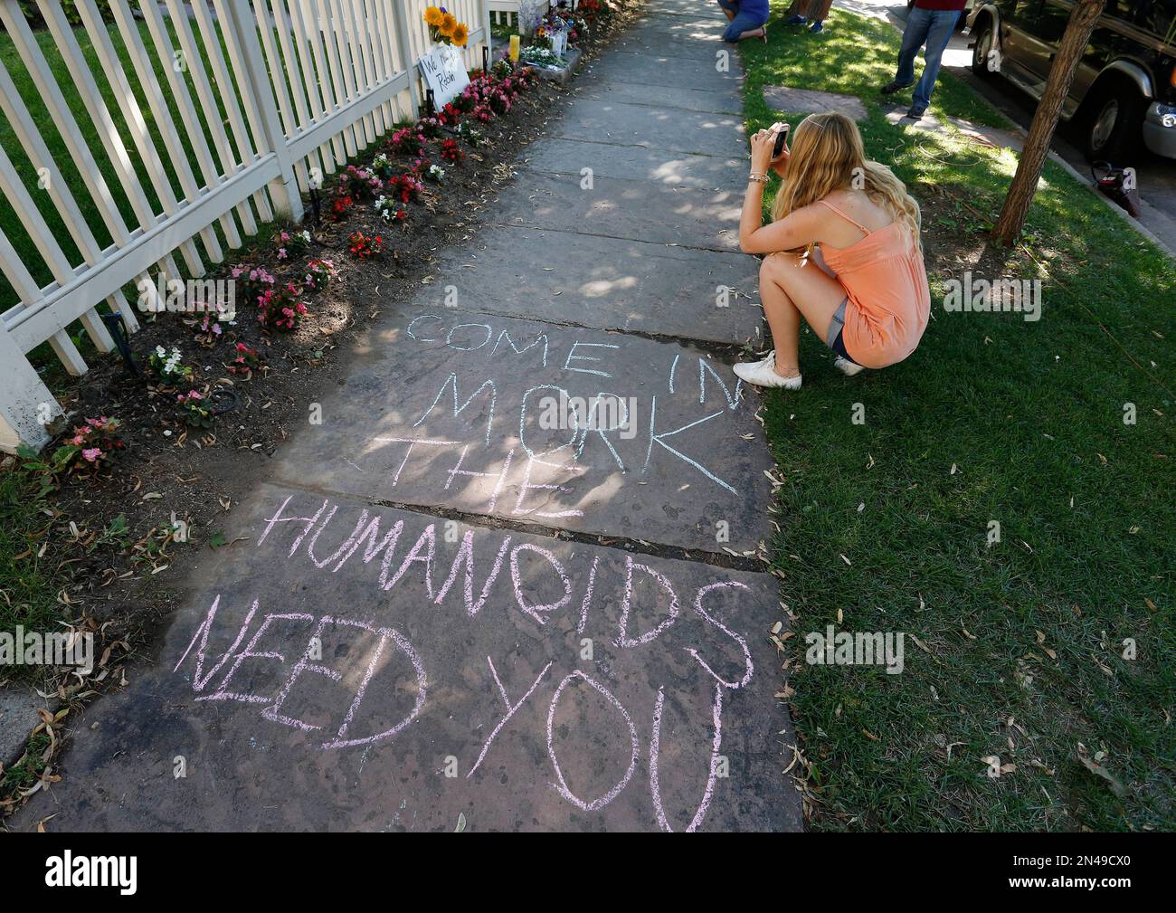 A woman takes a picture next to a sign written in chalk at a makeshift ...