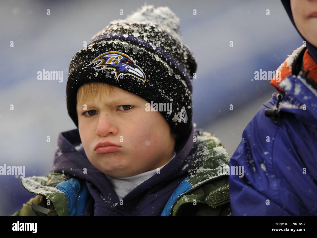 A young Baltimore Ravens fan watches players warm up as snow falls ...