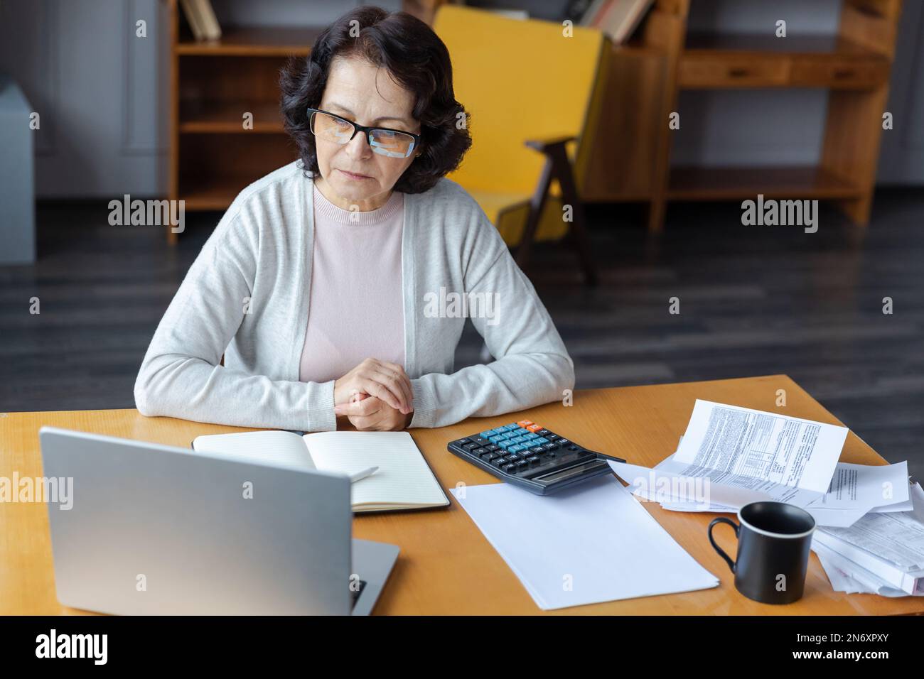 Eine ältere Frau im mittleren Alter sitzt mit einem Laptop und einem ...