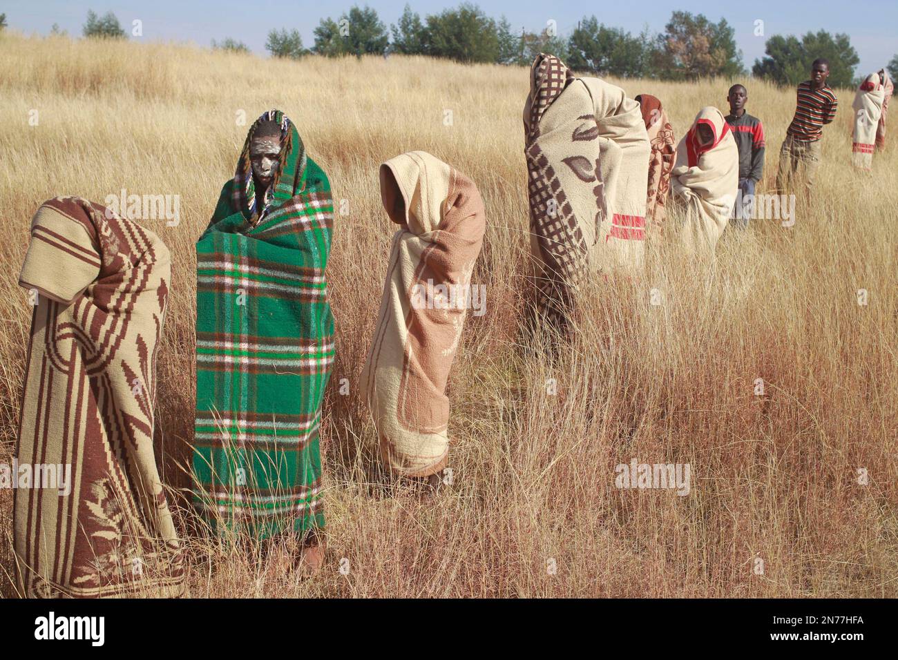 Xhosa boys covered with a blankets and smeared with chalky mud walk through a field as they ...