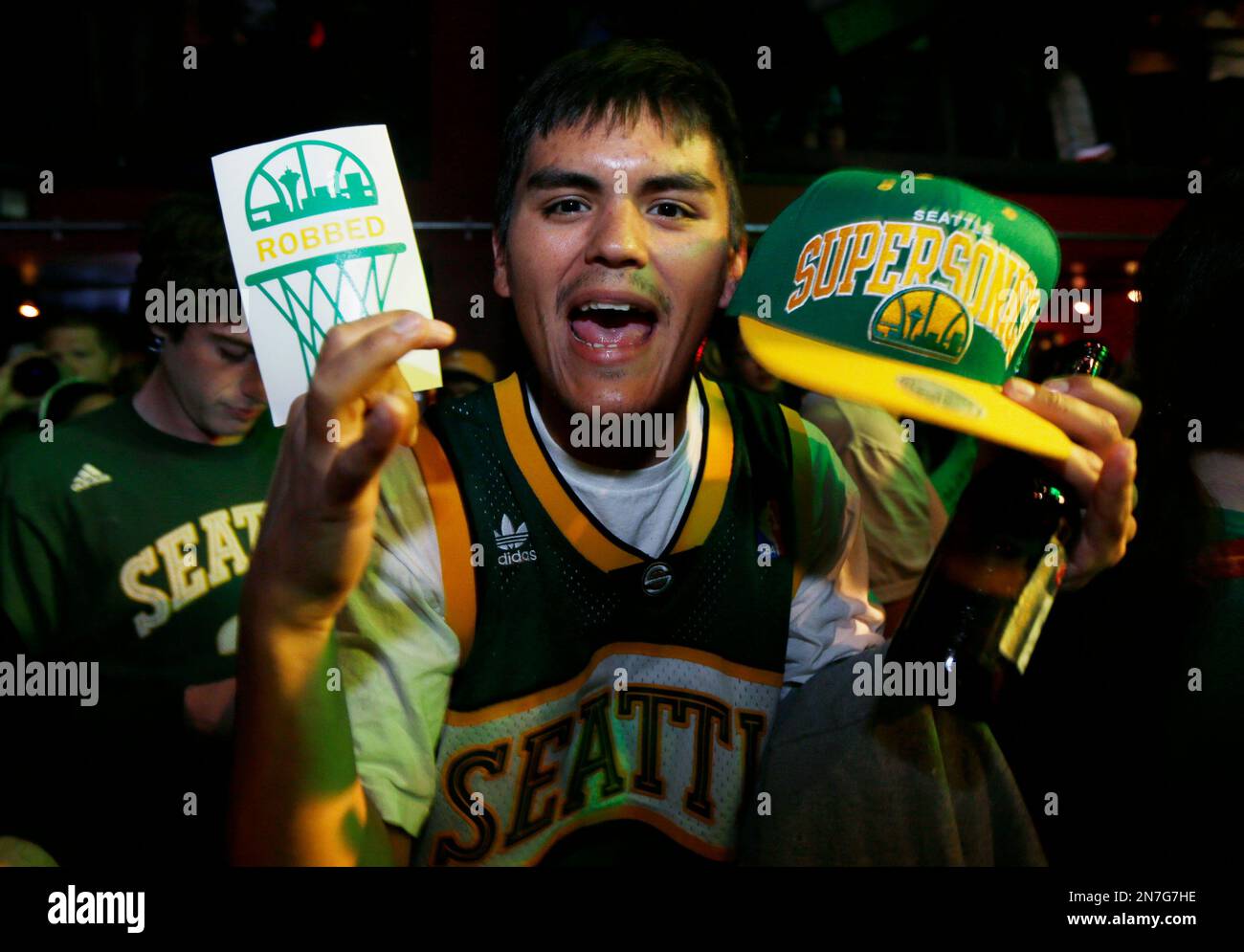 A fan holds a Seattle SuperSonics NBA basketball cap and a sign that ...
