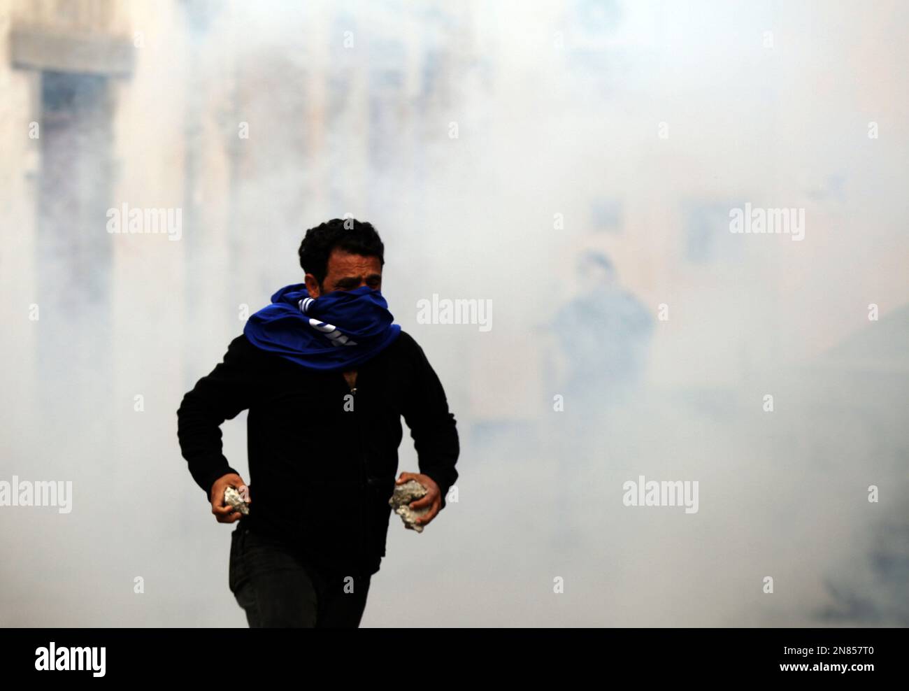 A masked Bahraini anti-government protester holding rocks runs through ...