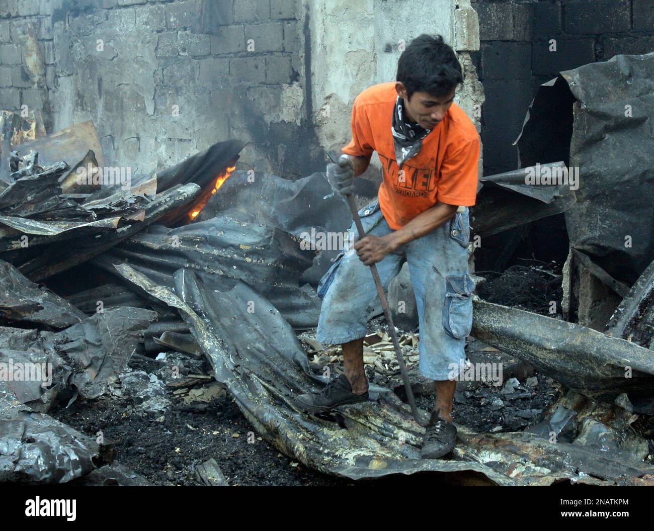 A man gathers corrugated sheets from his still smoldering house after a ...