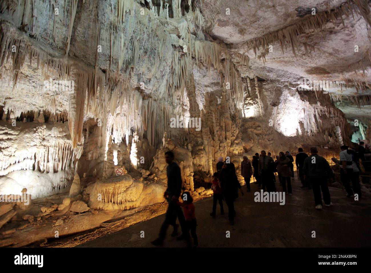 Tourists walk next to stalactites which are seen hanging in the upper ...