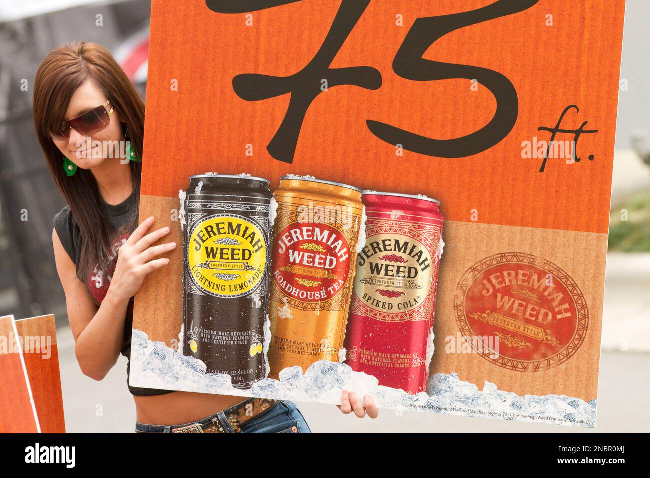 A Jeremiah Weed Premium Malt Beverages girl holds a sign before a ...