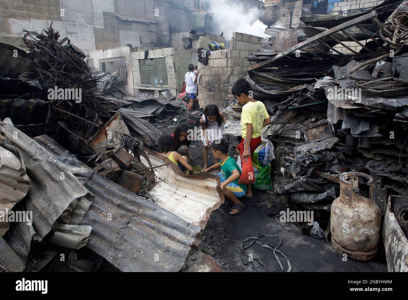 Children play beside a pile of burnt materials as residents return to ...