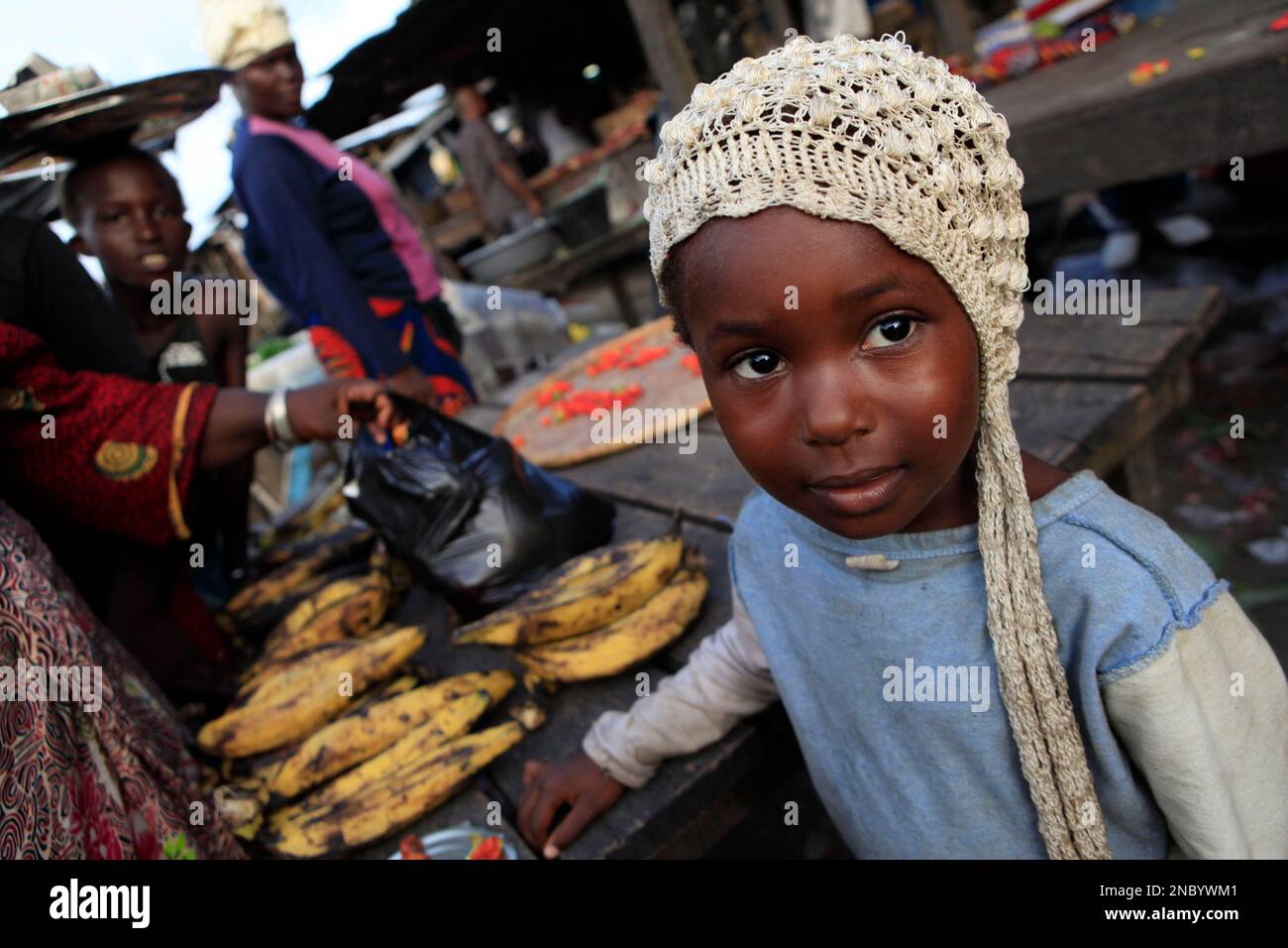 Fanta Bamba, 3, leans on her mother's fruit and vegetable stand, in a ...