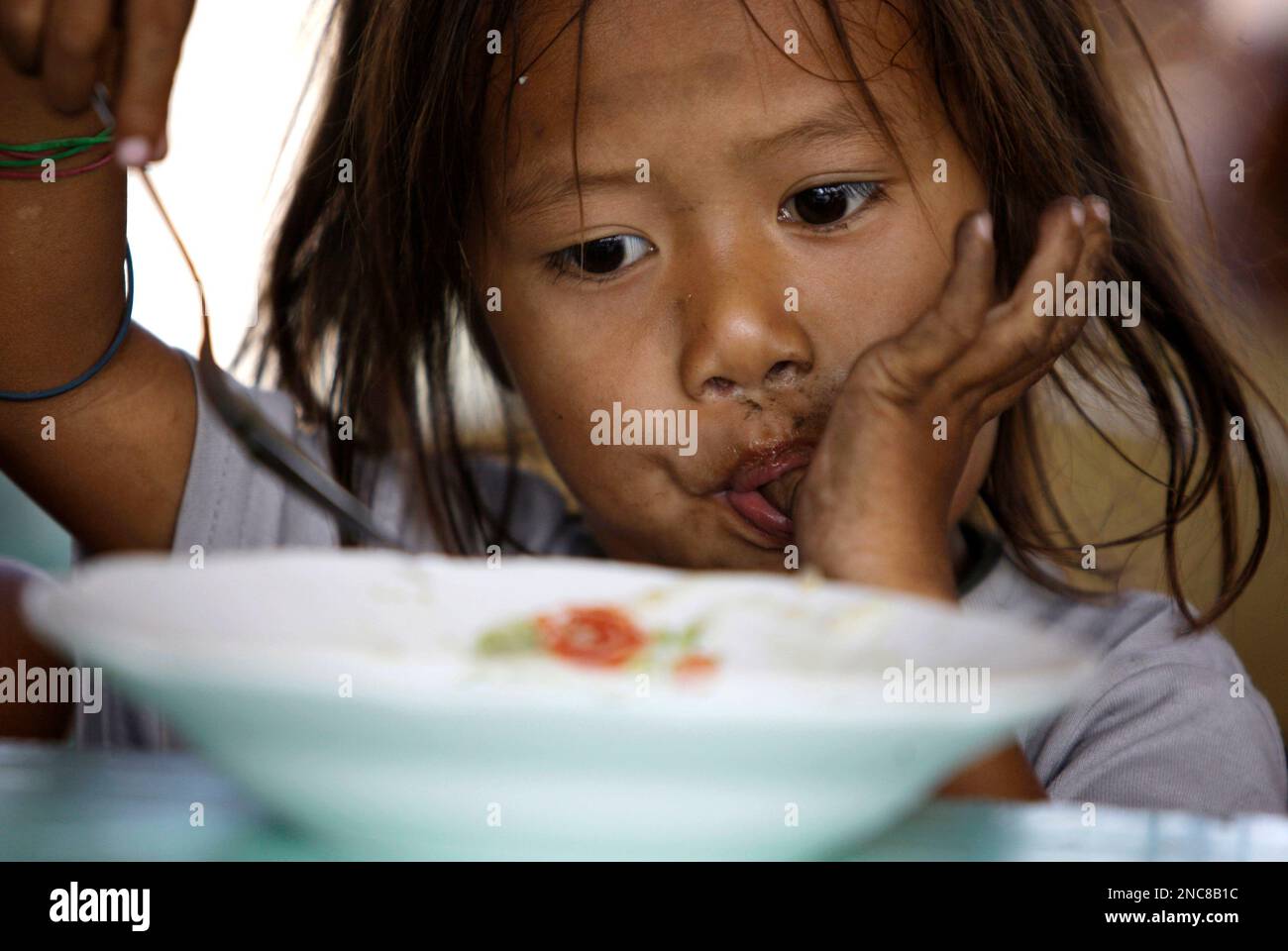 A Filipino girl sucks her thumb as she finishes the porridge that was ...