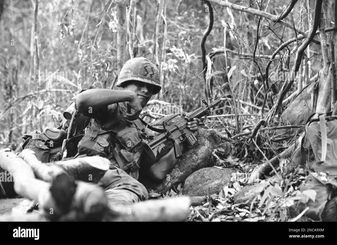 A paratrooper crouches behind rocks as he signals to members of his ...