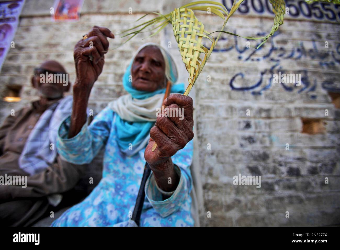 An elderly Pakistani Christian woman, holds a palm frond, while sitting ...
