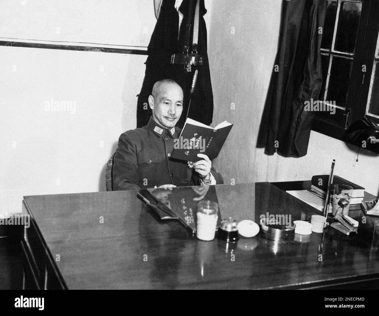 General Chiang Kai-Shek, seated at his desk in his office, reading a ...