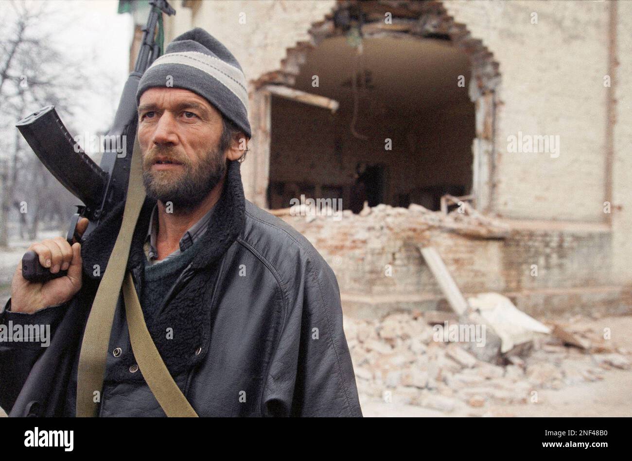 A Chechen fighter stands next to a building destroyed during clashes ...