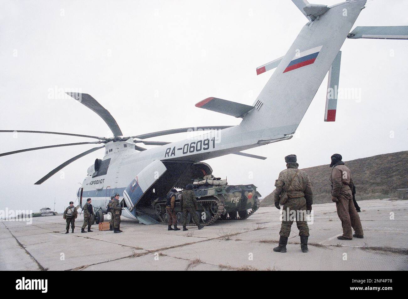 Soldiers stand by while an APC is loaded onto a MI-26 cargo helicopter ...