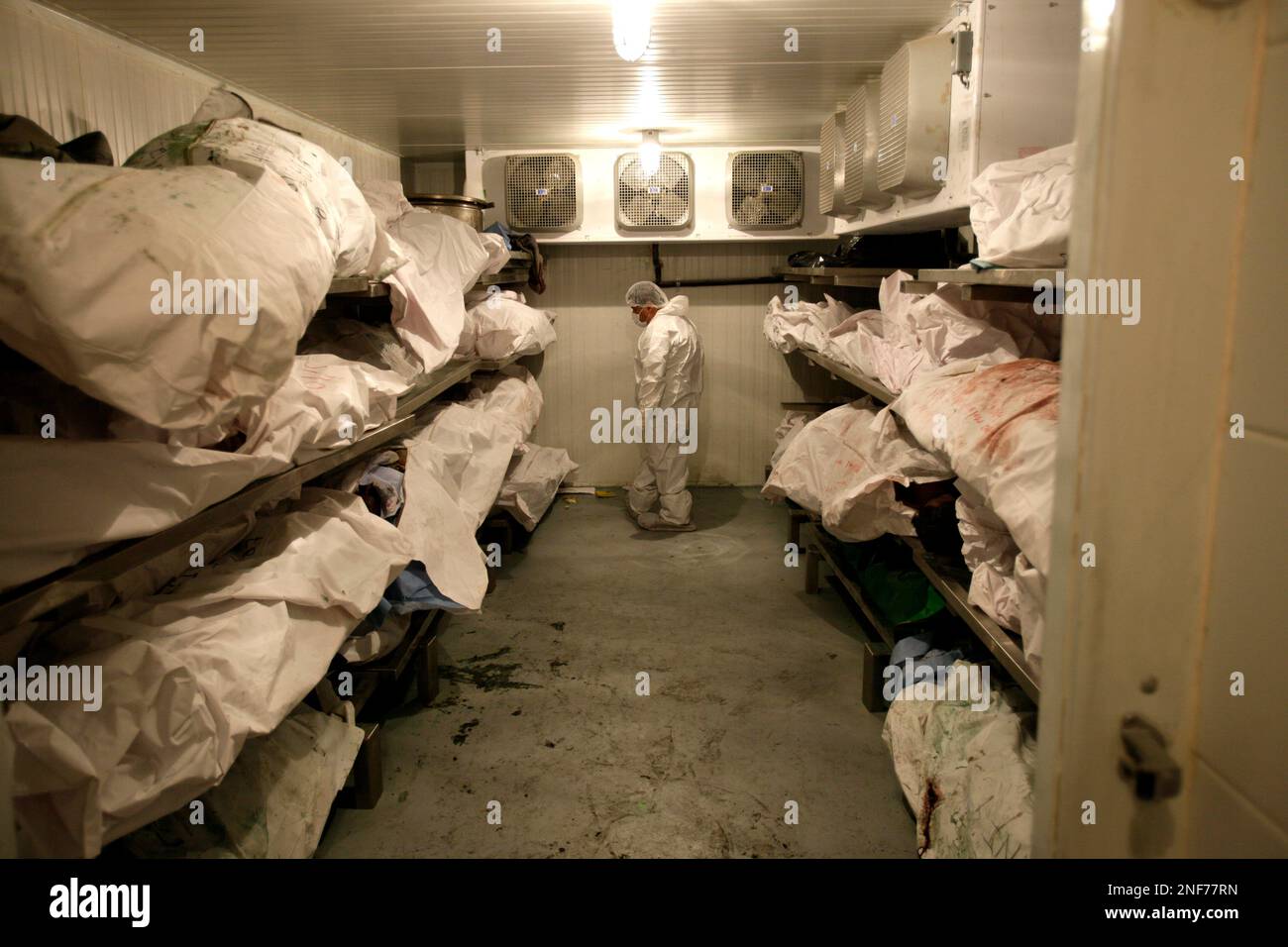 A forensic worker stands inside a walk-in refigerator stacked with ...