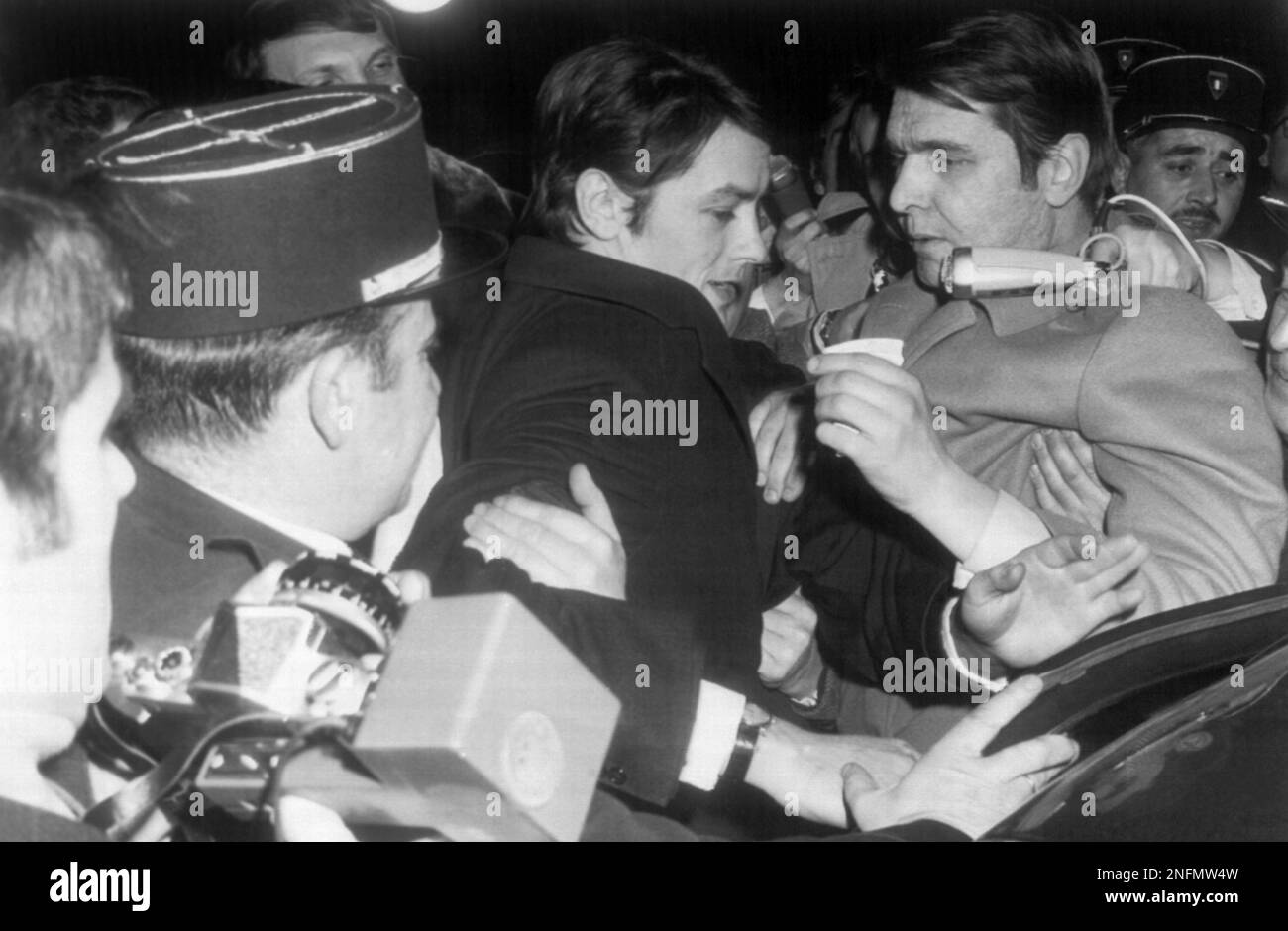 Gendarmes help French actor Alain Delon center through a mob of newsmen ...