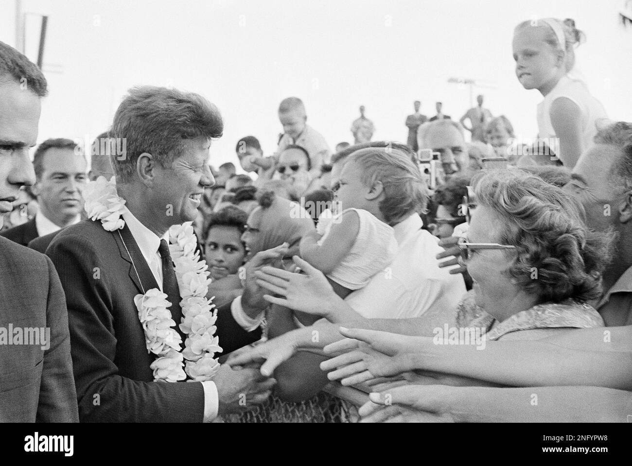 President John Kennedy, with a floral lei around his neck, waves ...