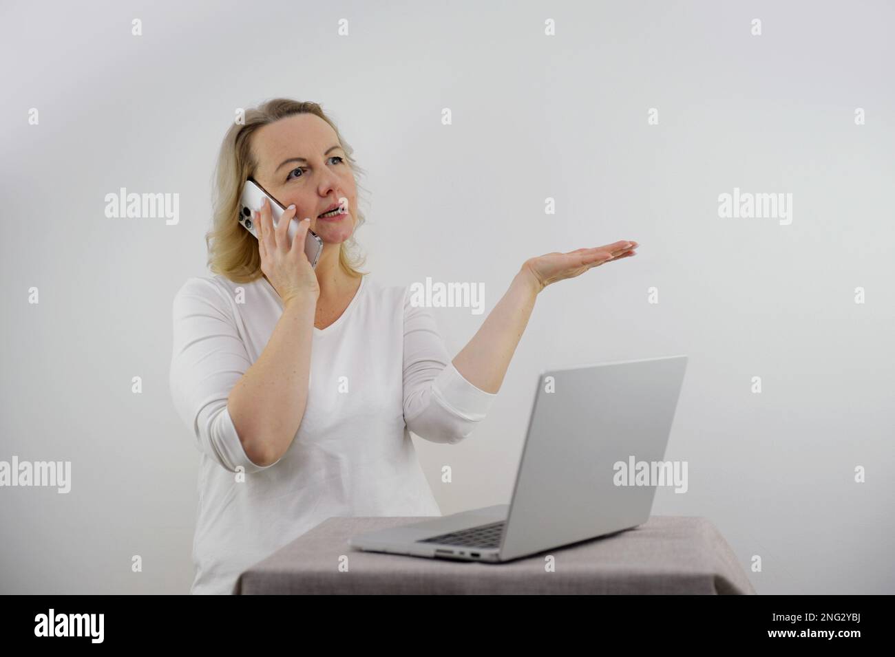 Frau, die telefoniert und mit der Hand auf den Laptop-Tisch zeigt ...