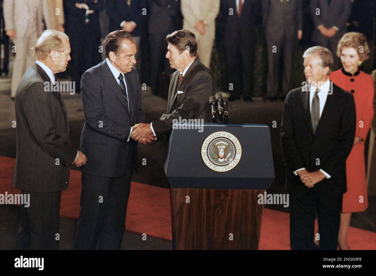 U.S. President Ronald Reagan, behind podium, shakes hands with former ...