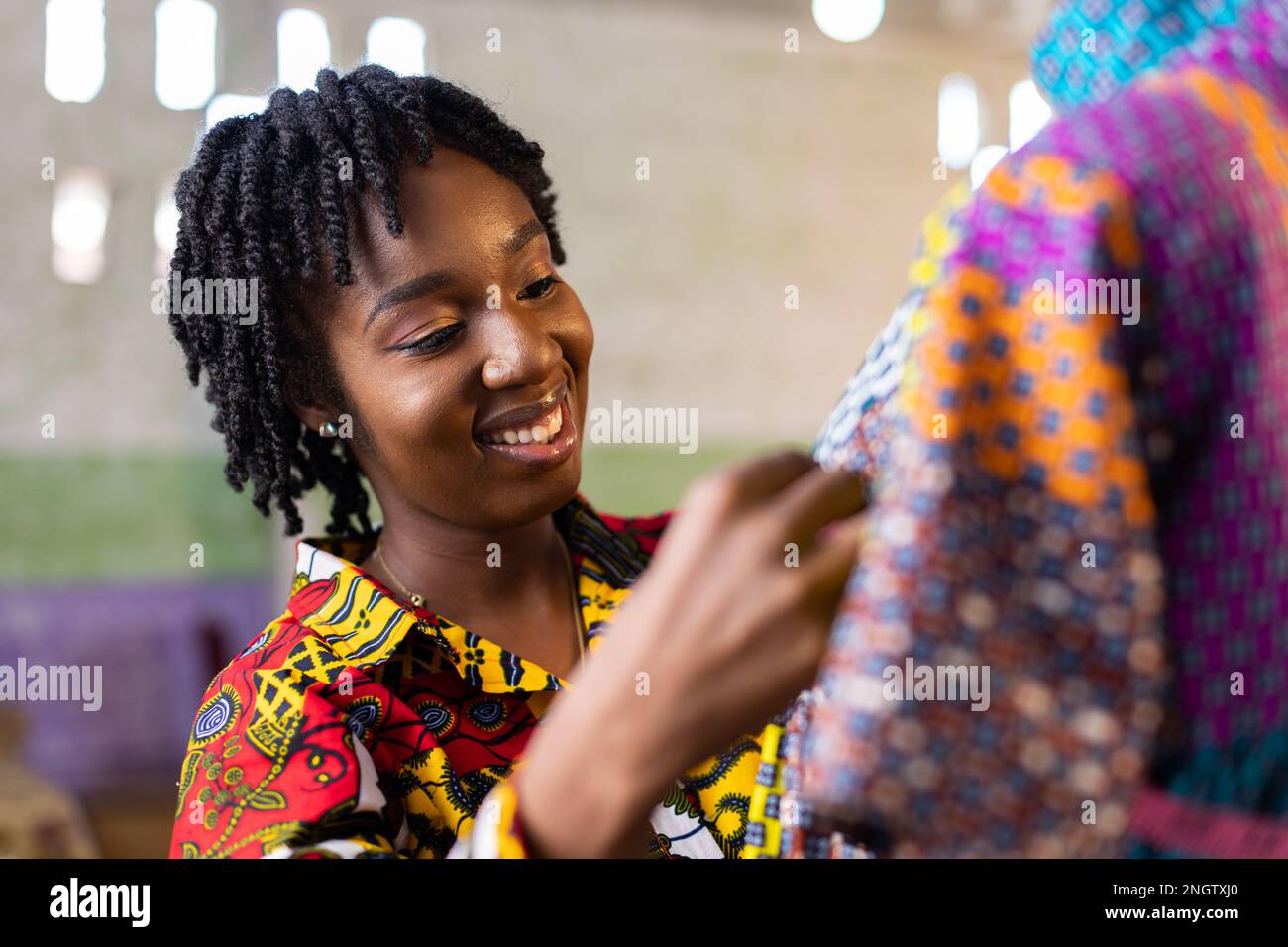 Eine lächelnde westafrikanische Schneiderin mit haaren von locs misst ...