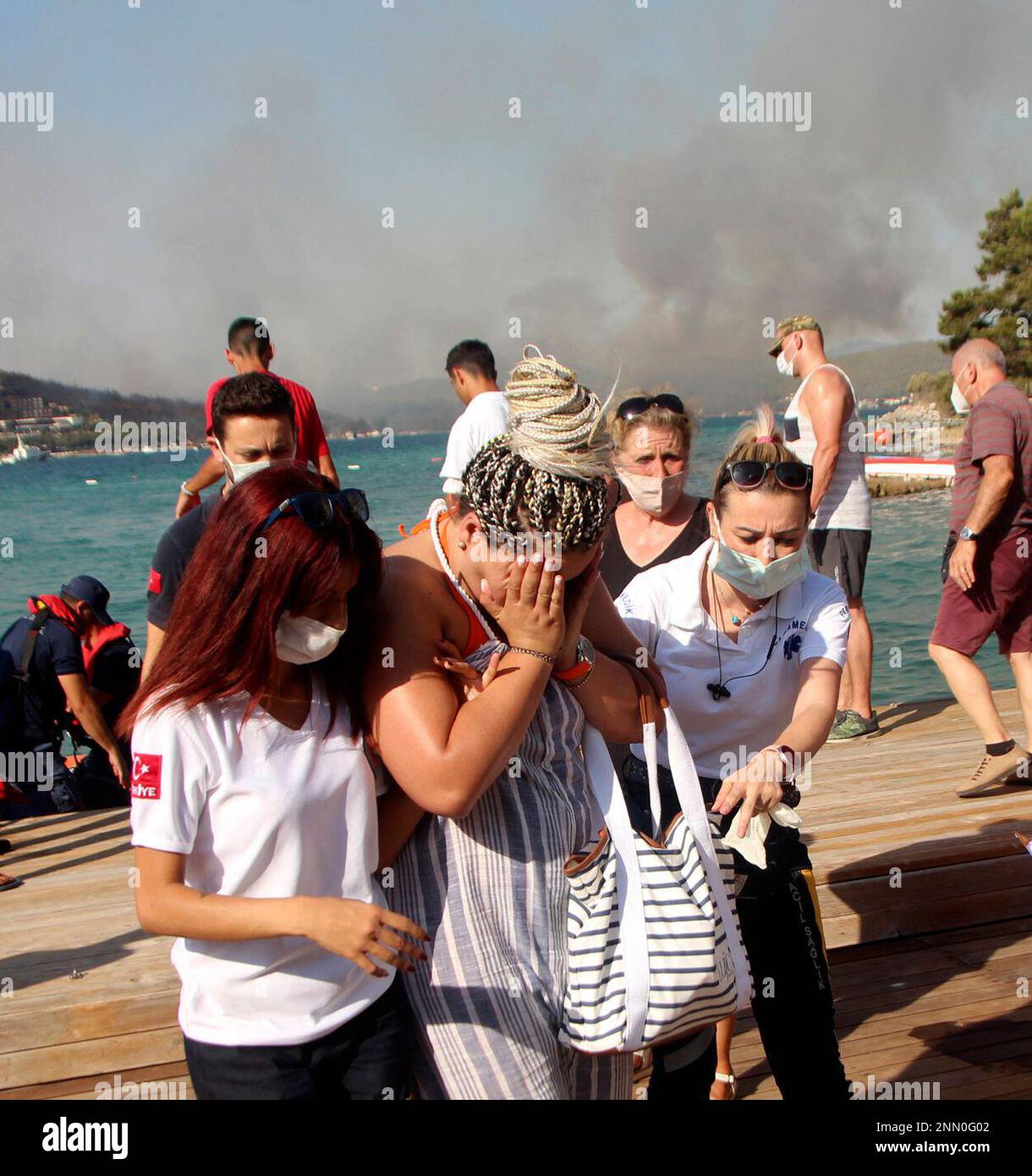 Medics help an evacuated woman as smoke rises from a forest fire ...