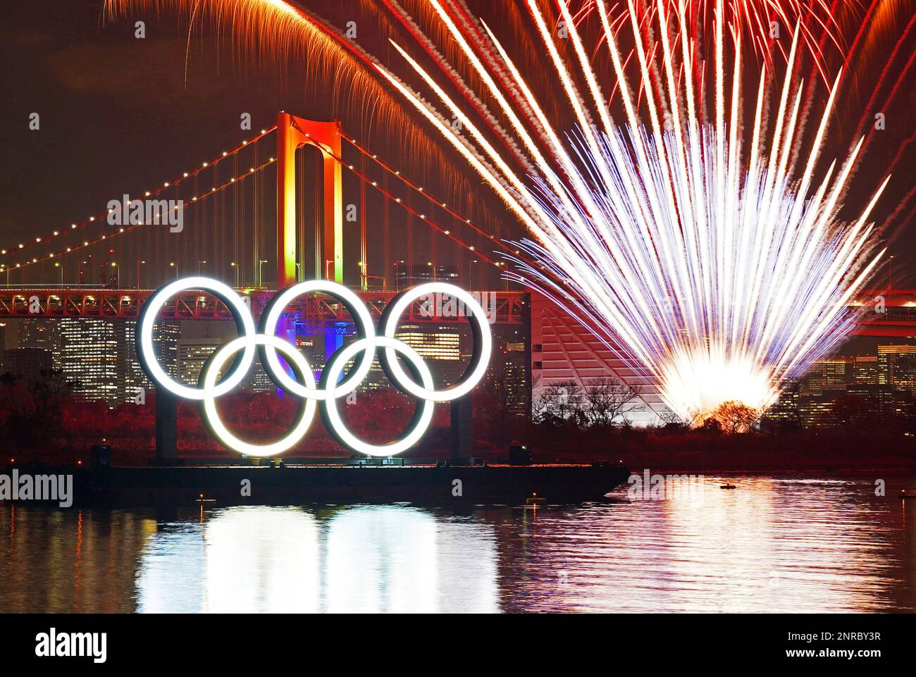 A monument of five-ring emblem is lit up on the water with fireworks to ...